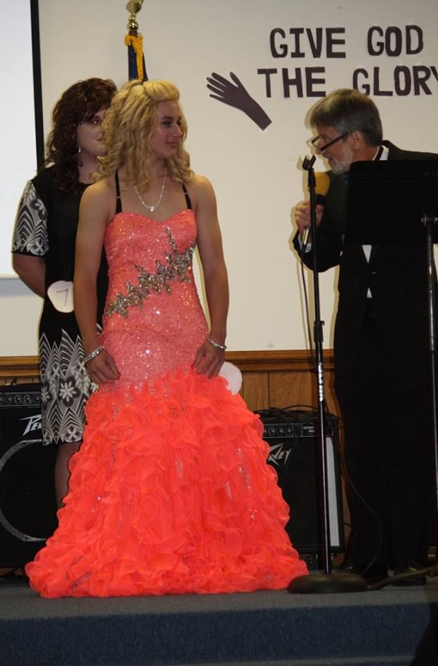 A Woman In An Orange Dress Standing On Stage With Two Men Behind Her