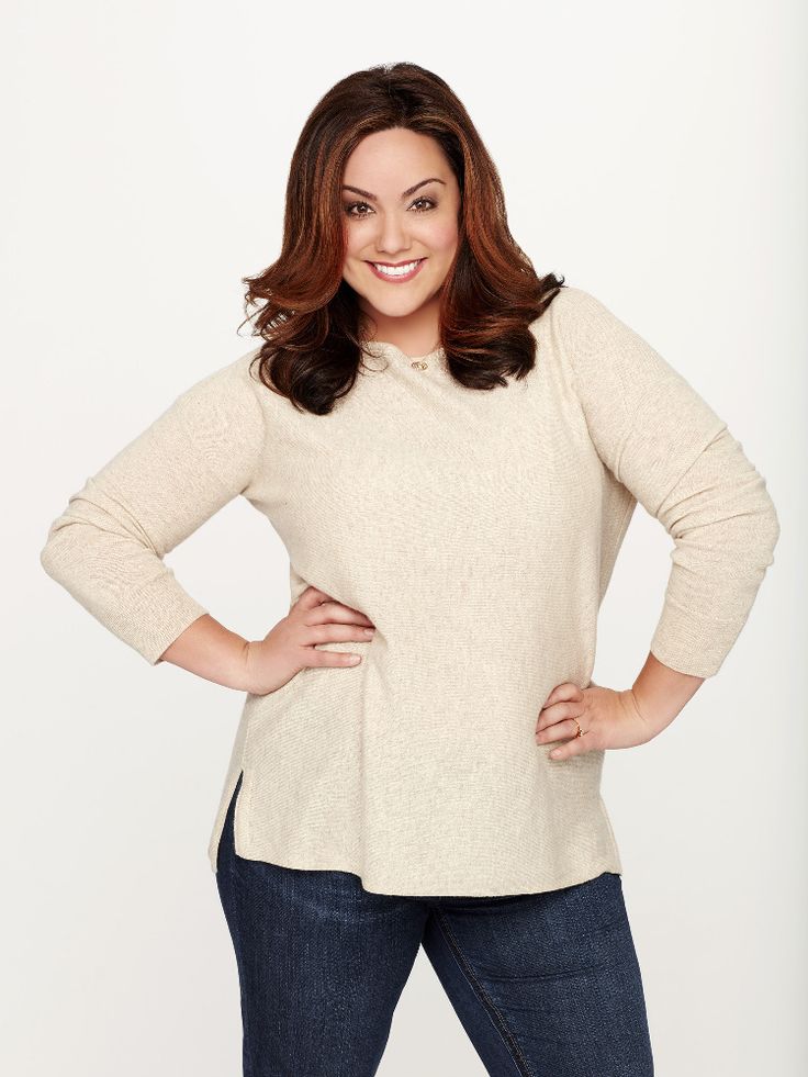 A Woman Standing With Her Hands On Her Hips And Smiling At The Camera While Wearing Jeans