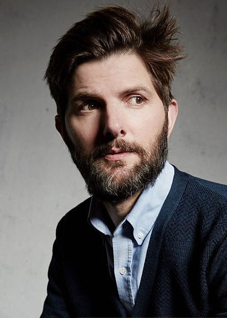 A Man With A Beard Wearing A Blue Shirt And Cardigan Is Looking At The Camera