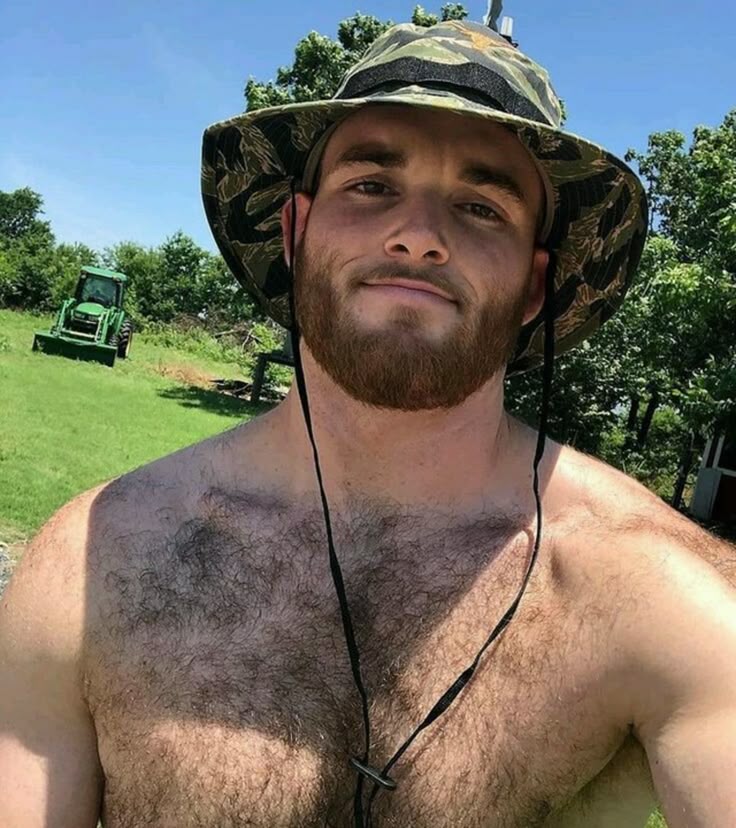 A Shirtless Man Wearing A Hat And No Shirt Standing In The Grass With His Hands On His Hips