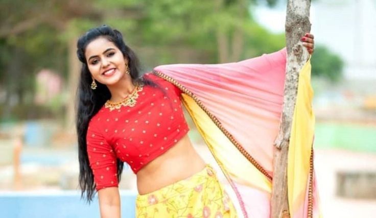 A Woman In A Red And Yellow Sari Posing For The Camera With Her Arms Around A Tree