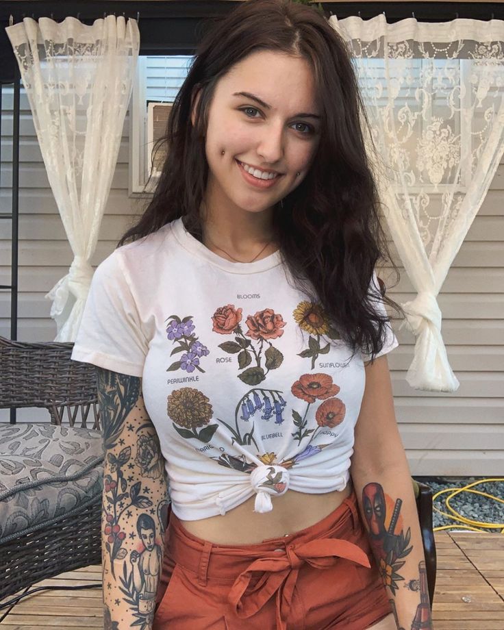 A Woman With Tattoos On Her Arms And Chest Sitting In Front Of A Window