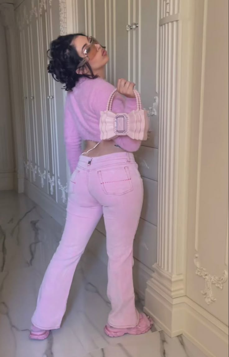 A Woman In Pink Is Leaning Against A Wall With Her Hand On The Back Of Her Purse