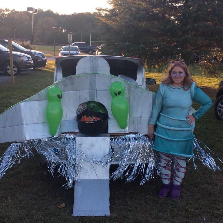 A Woman Standing In Front Of A Fake Car With Two Green Birds On Its Hood