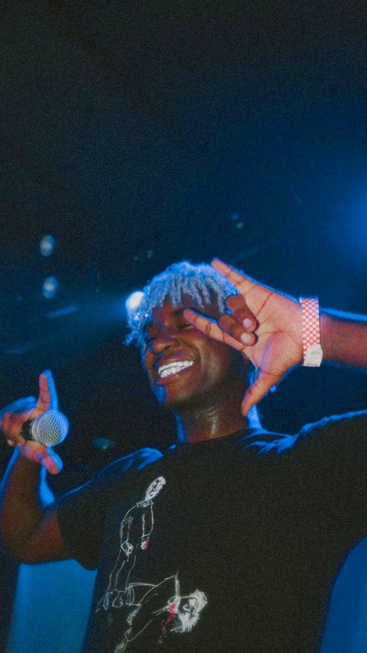 A Man Holding His Hand Up In The Air While Singing Into A Microphone At A Concert