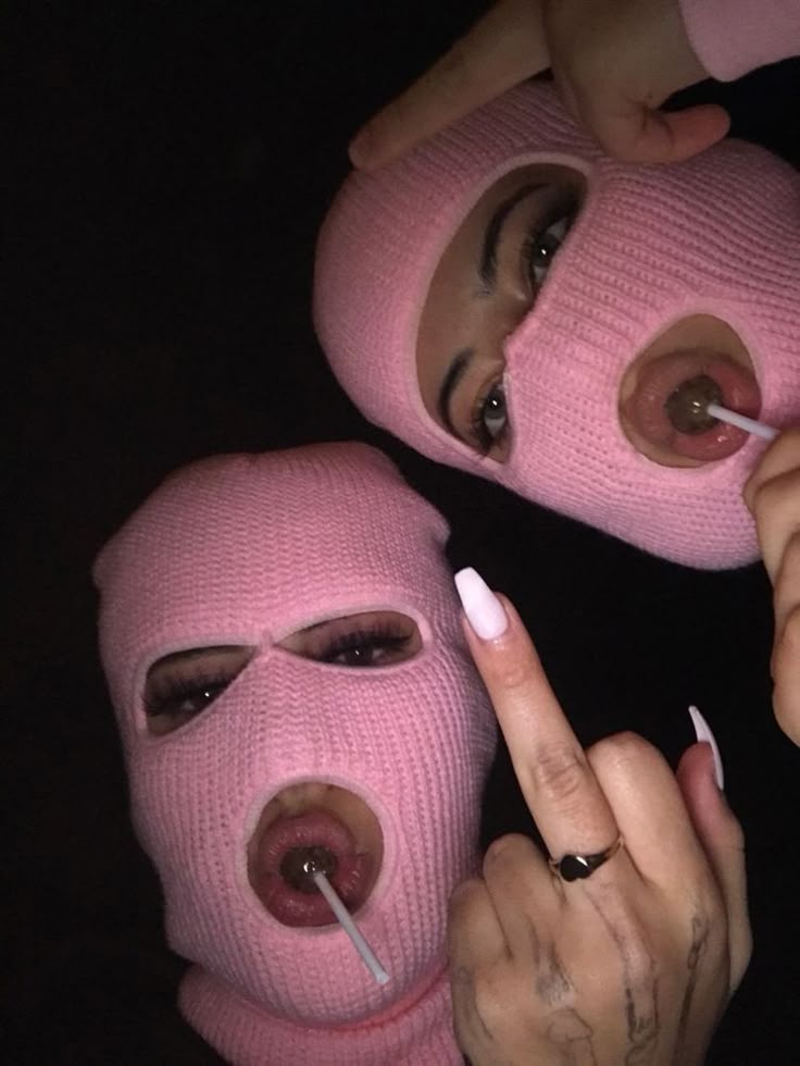 Two Women Wearing Pink Masks With One Pointing At The Others Nose And