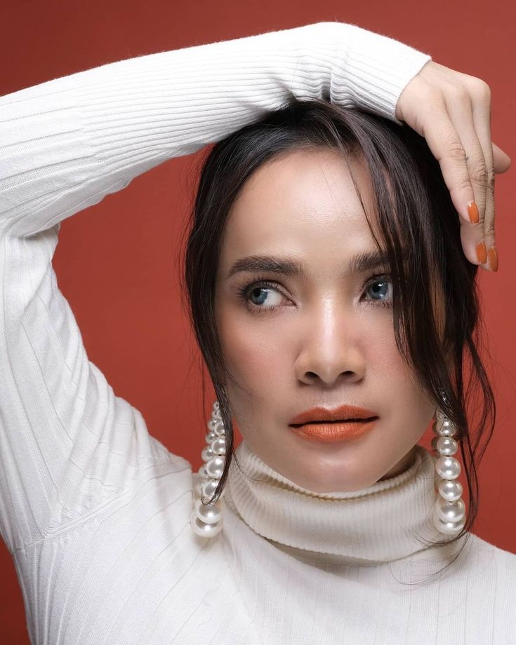 A Woman With Her Hands On Her Head And Wearing Pearls Around Her Neck Posing For The Camera