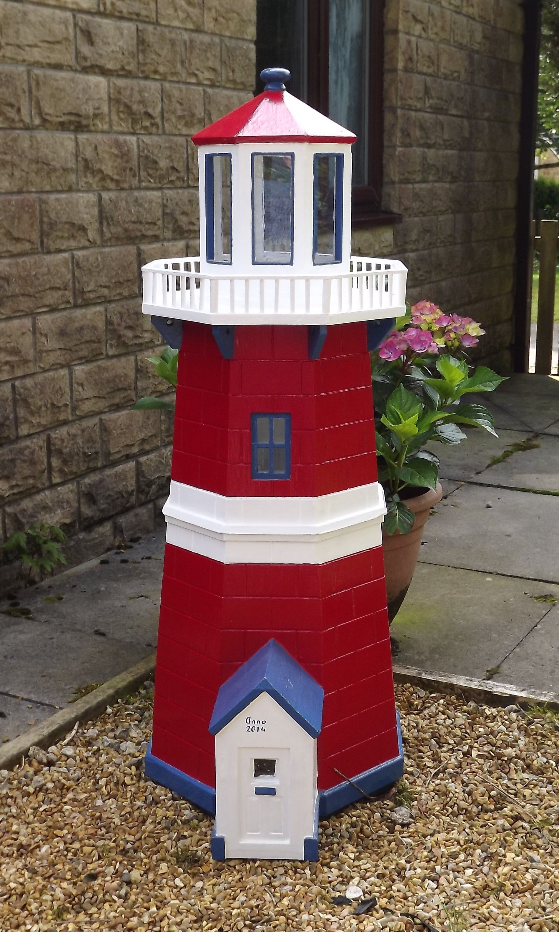 A Red And White Lighthouse Sitting In Front Of A Brick Building Next To A Potted Plant