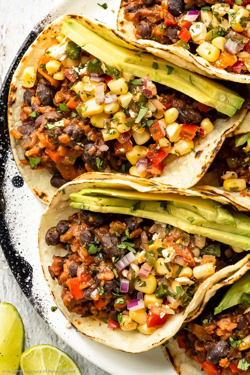 Overhead Close Up Photo Of Black Bean Tacos Topped With Corn Salsa And Slices Of Avocado On A