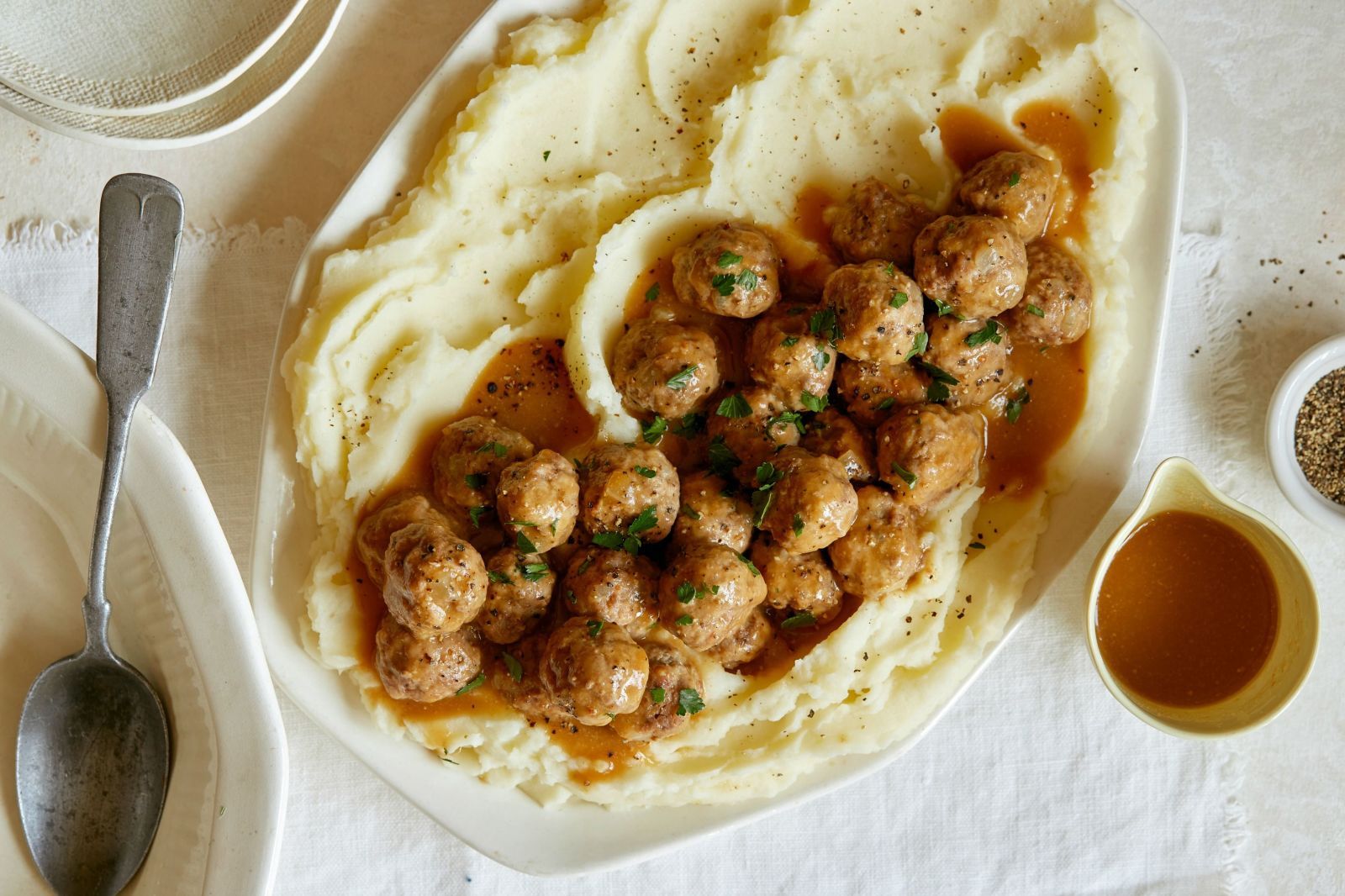 Mashed Potatoes With Meatballs And Gravy On A White Plate Next To Two